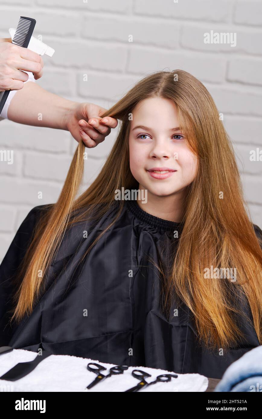 Hairdresser making a hair to cute girl in hair salon. Young girl at ...