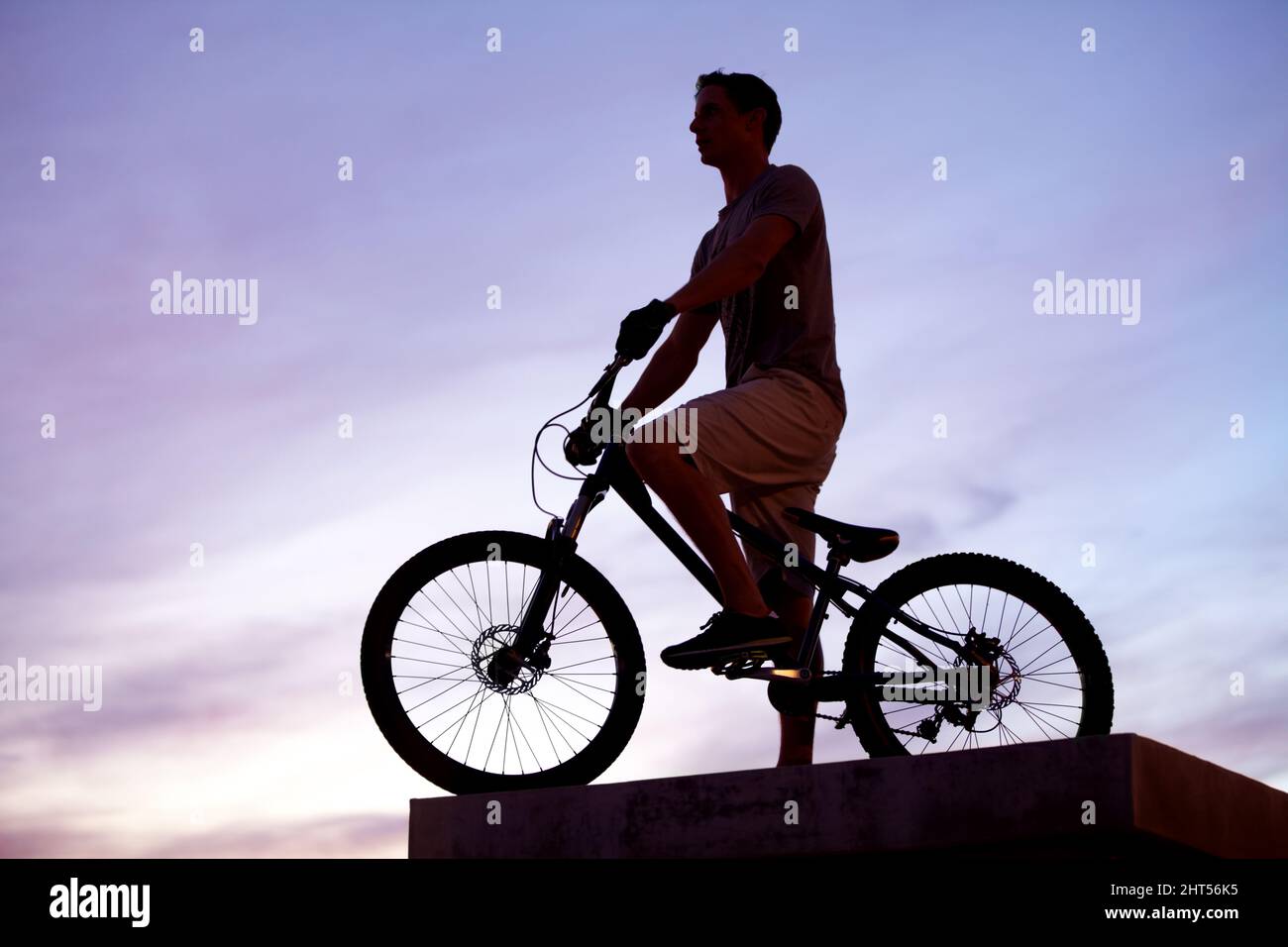 King of the city. Silhouette shot of a man riding his bike at dusk ...