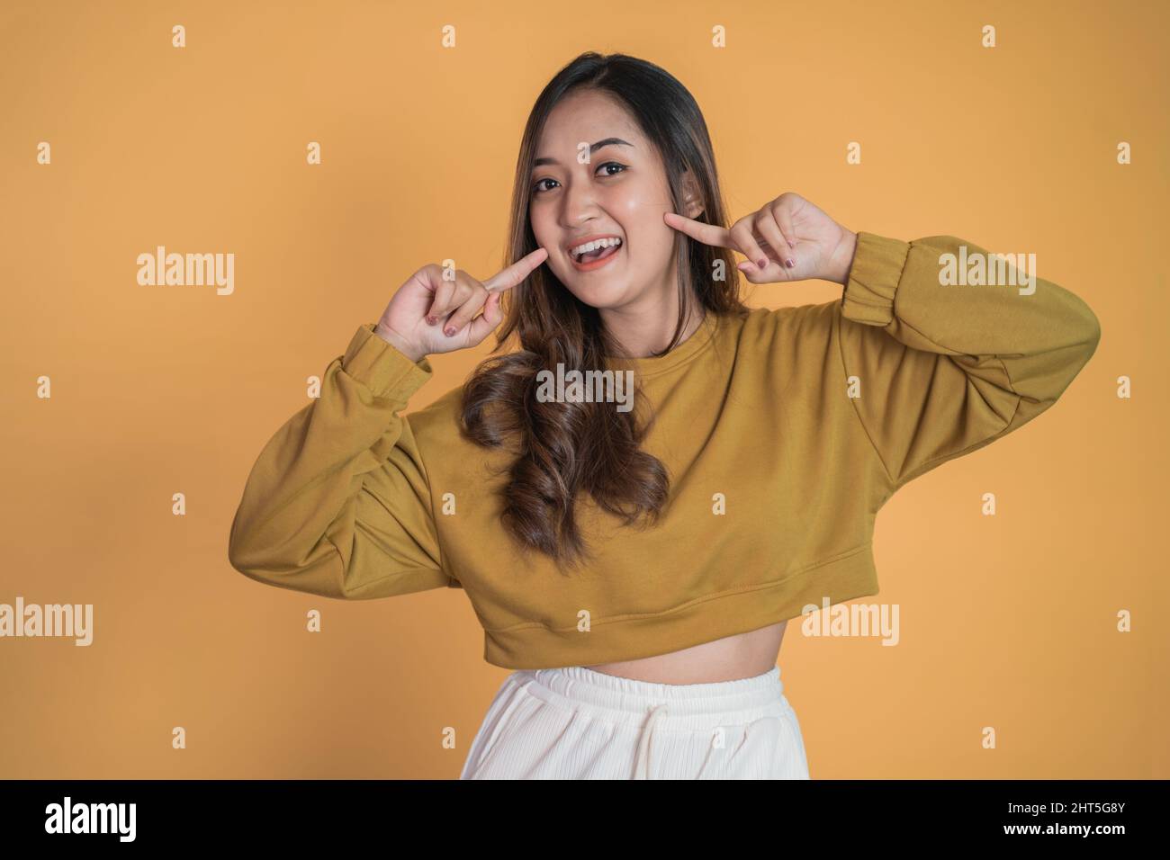 Smiling cute young woman with two fingers pointing to cheek Stock Photo ...