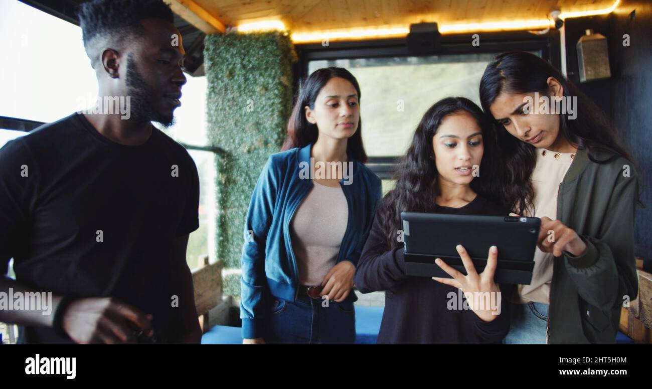 Group of young South Asian friends looking at a tablet in a cafe in ...
