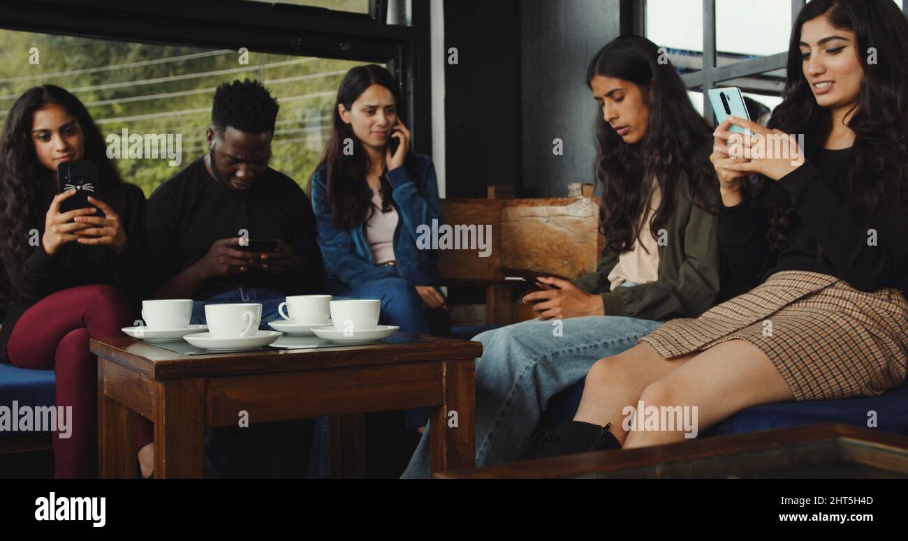 Group of South Asian friends focused on their smartphones in a cafe in ...