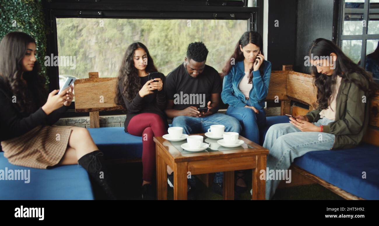 Group of South Asian friends focused on their smartphones sitting in a ...