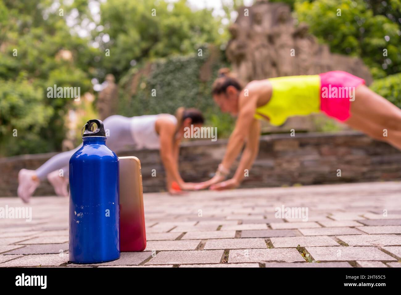 Selective focus shot of a water bottle and a phone with two women doing ...