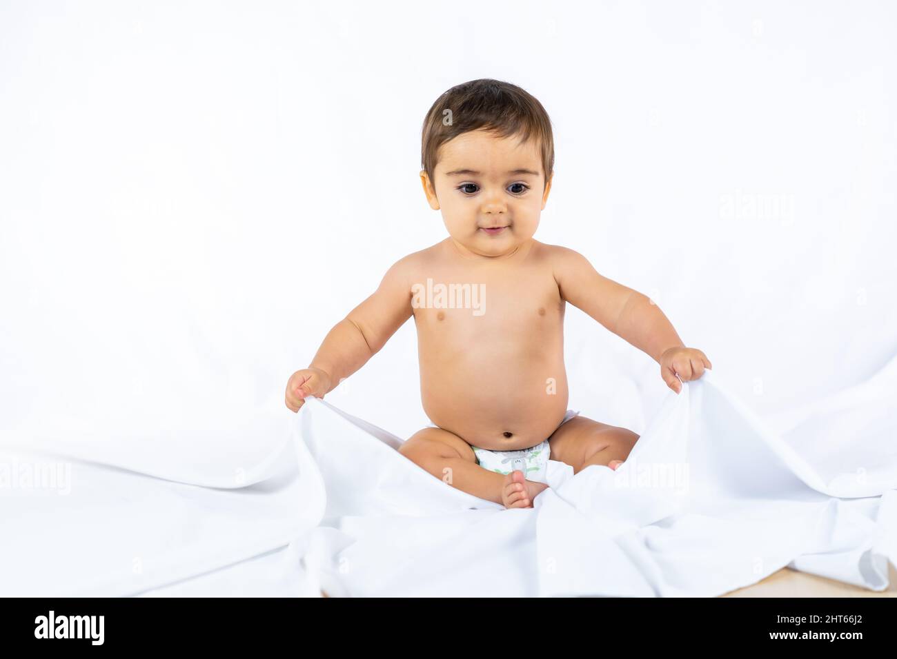Cute caucasian baby boy sitting in a diaper on a cloth against white ...