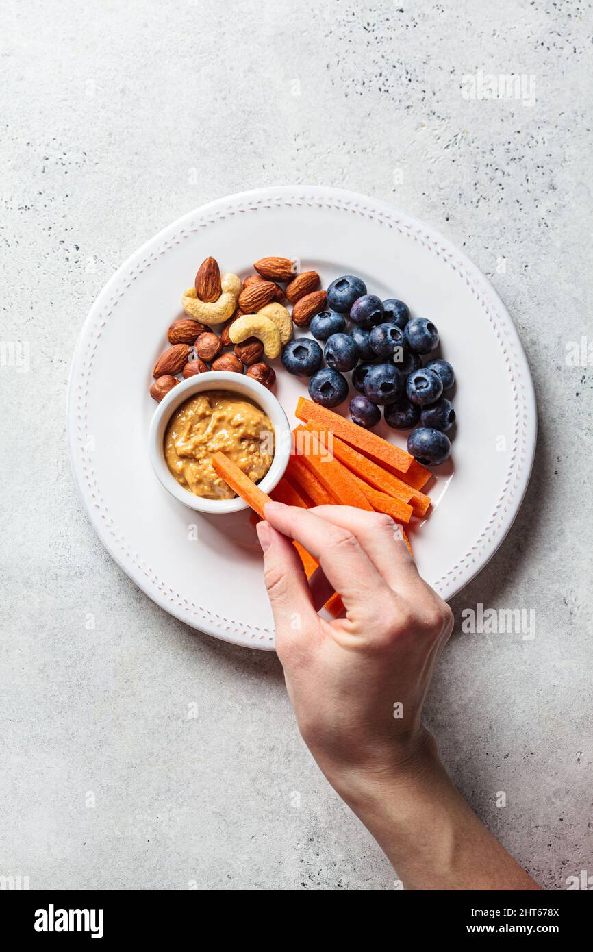 Woman hand eating healthy snacks plate - carrots, nuts, berries and ...