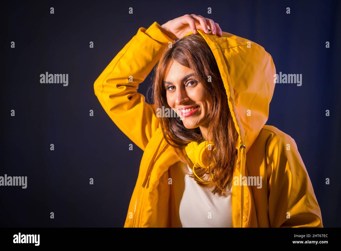 Young brunette Caucasian with headphones and yellow jacket smiling at ...