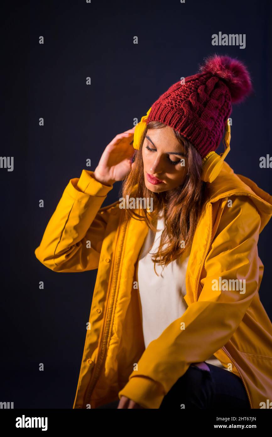 Young Caucasian girl with headphones, yellow jacket and wool hat ...
