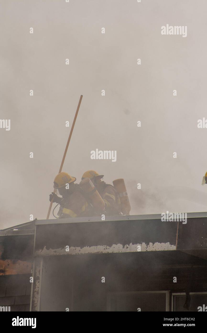 Vertical photo of firefighters extinguishing a fire on a roof of a ...