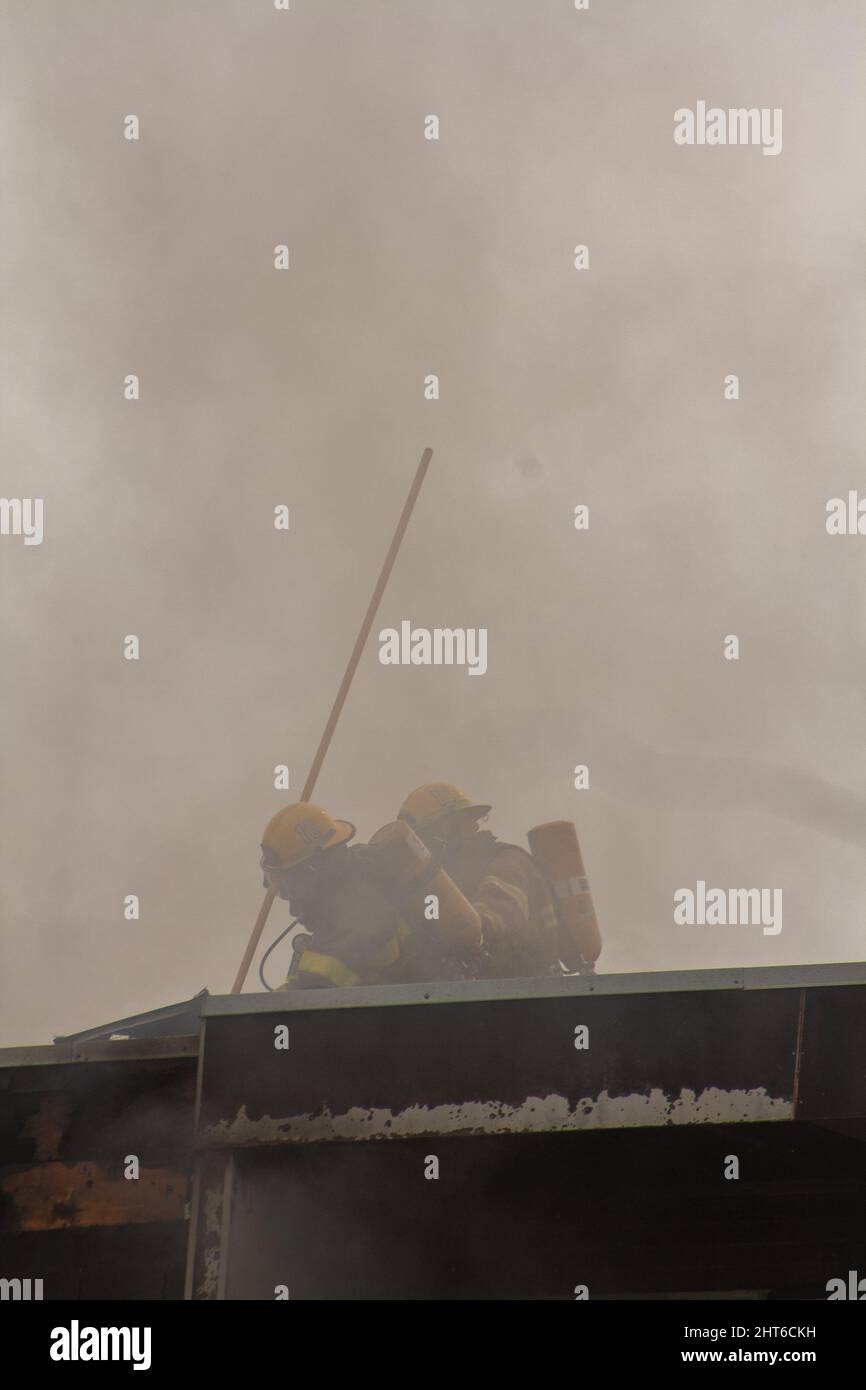 Vertical photo of firefighters extinguishing a fire on a roof of a ...