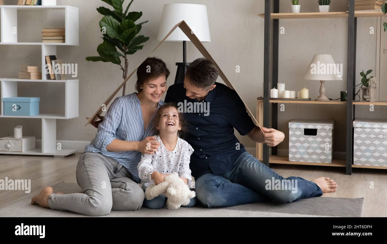 Happy young parents and little daughter sitting under carton roof Stock ...