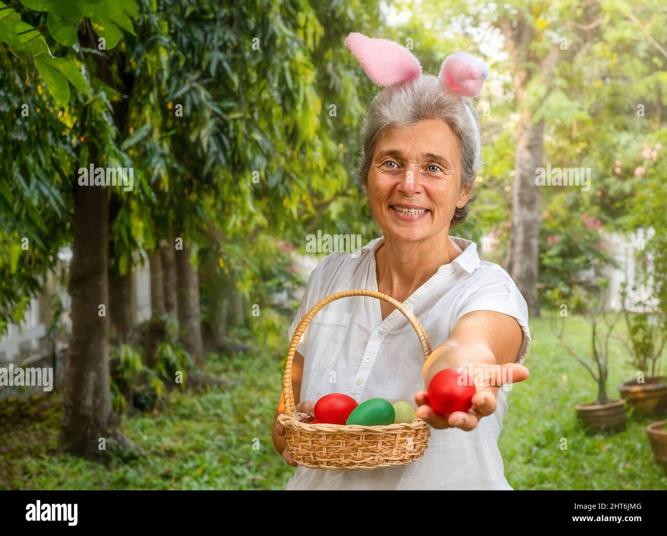 Senior woman holding out Easter basket with eggs in the backyard Stock ...