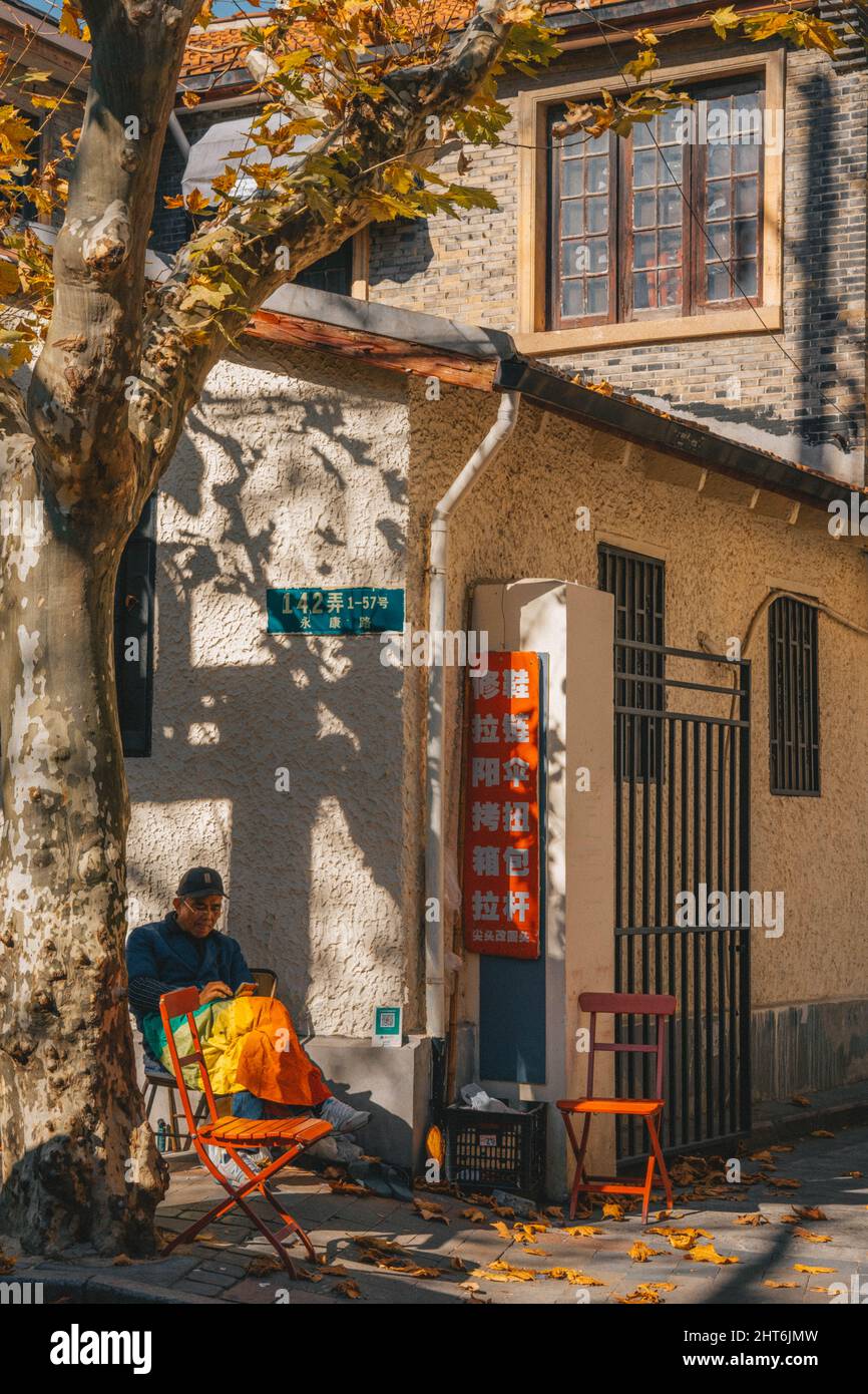 Old man sitting in the street under the tree shadow on an autumn sunny ...