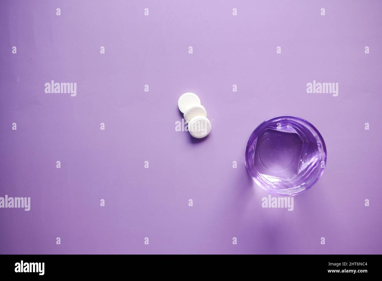 Effervescent soluble tablet pills and glass of water on purple ...