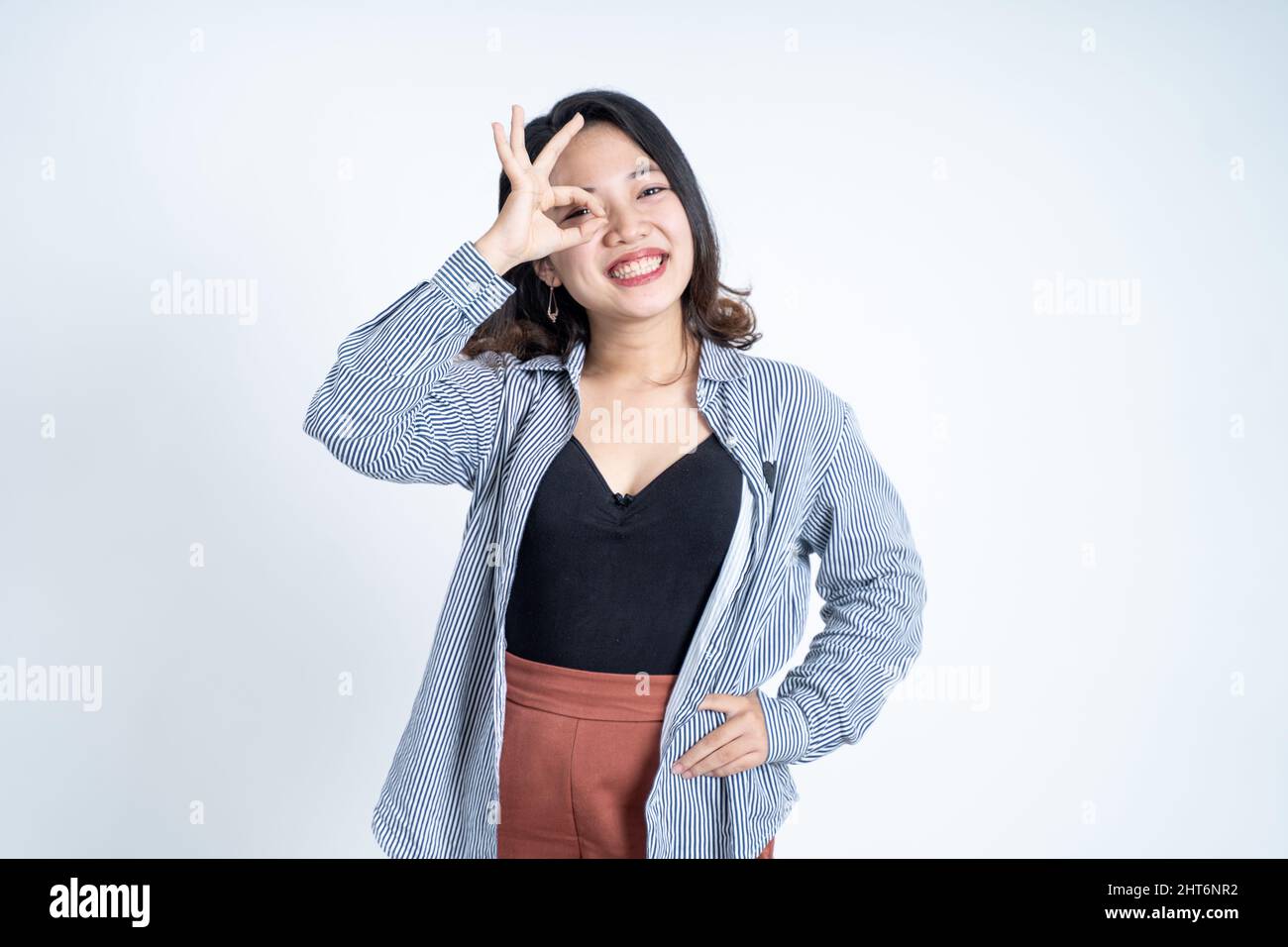 Young woman showing oke gesture with eye looks imitating binoculars ...
