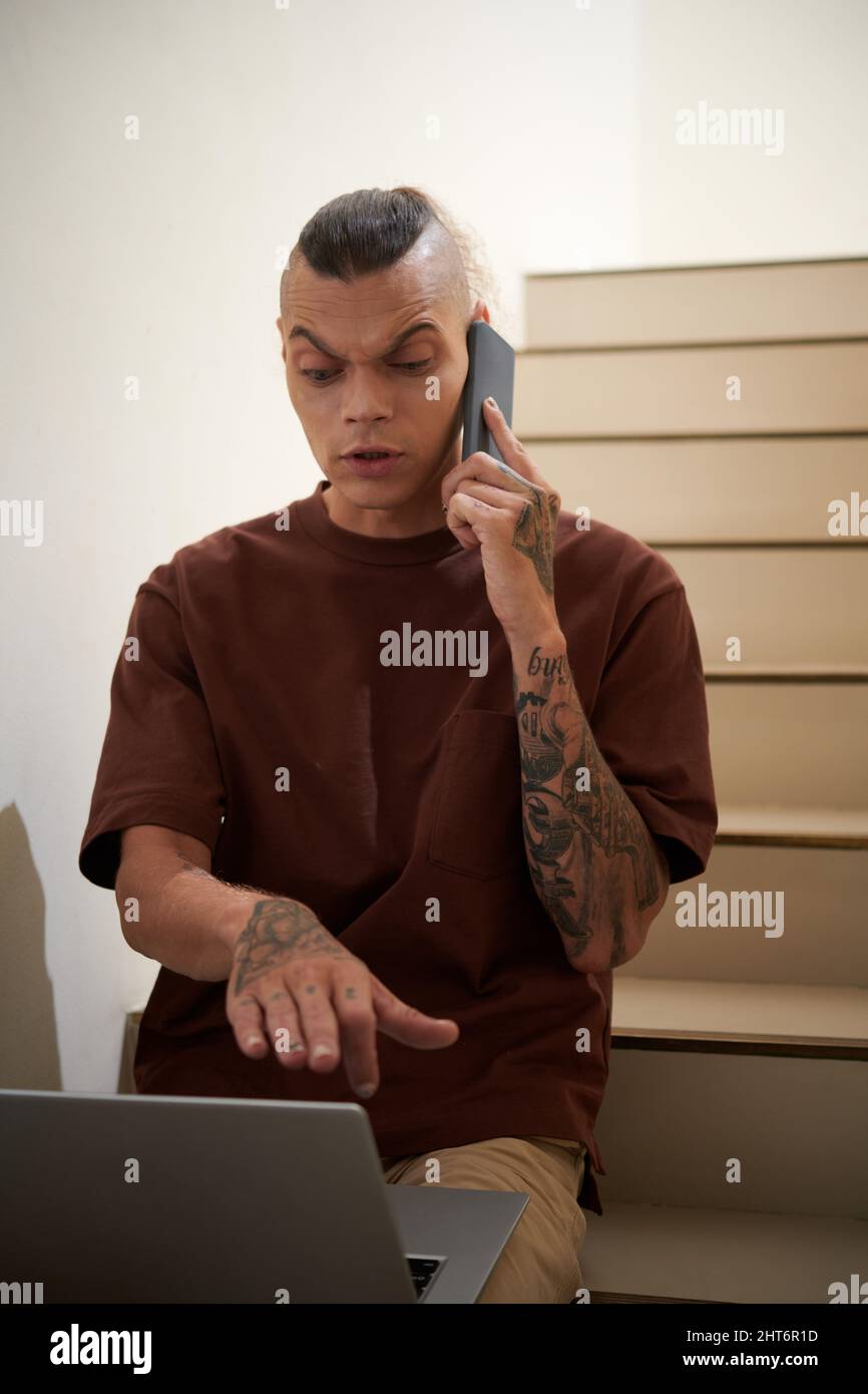 Emotional young man sitting on steps and talking on phone with ...