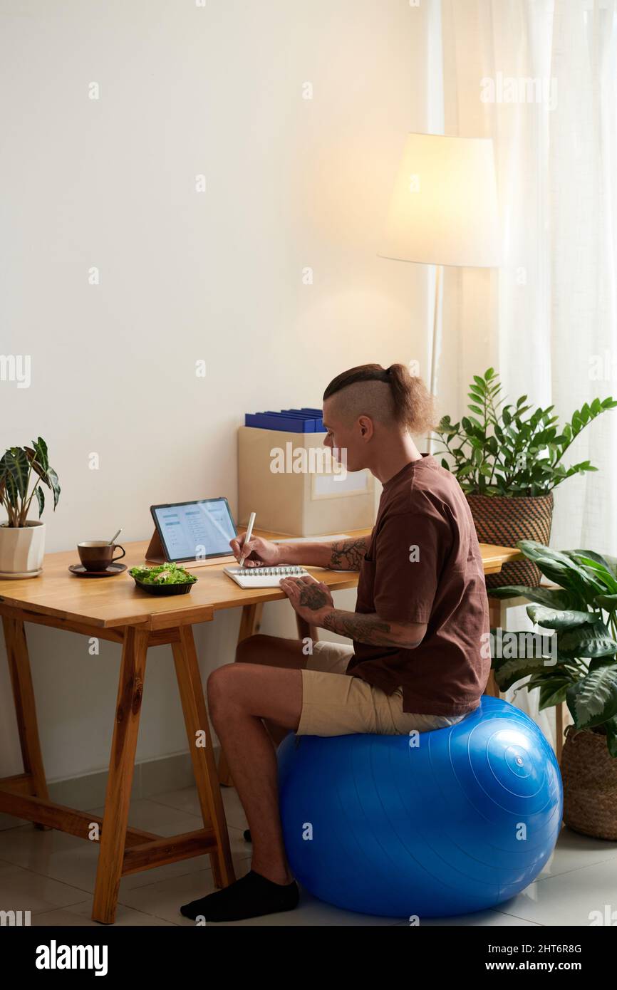 Freelancer sitting on fitness ball at his desk in home office and ...