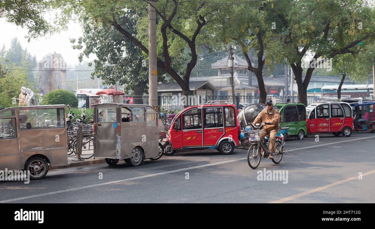 A man cycles past a row of parked electric three-wheeler taxis near Tao ...