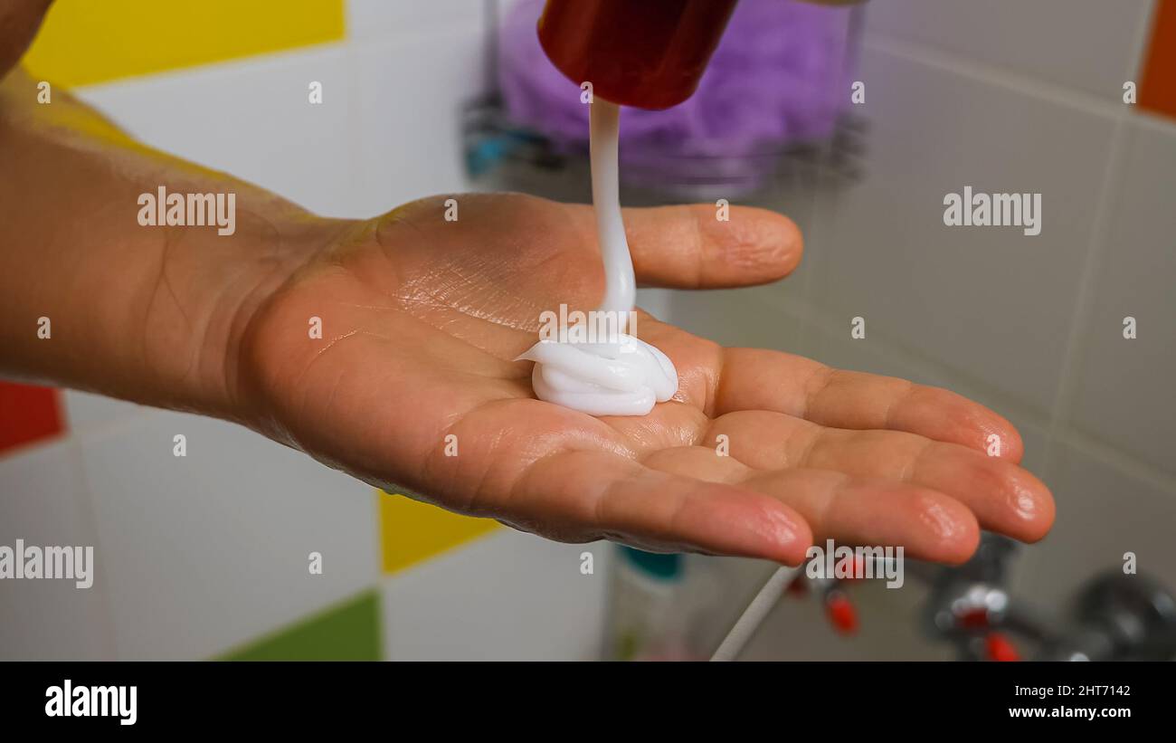 A close-up of white hair conditioner pouring out of a tube onto a woman ...