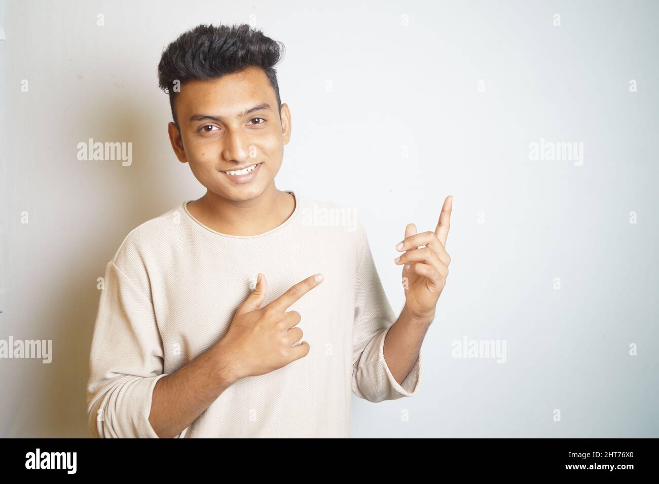 Young South Asian guy wearing a beige shirt pointing to the left ...