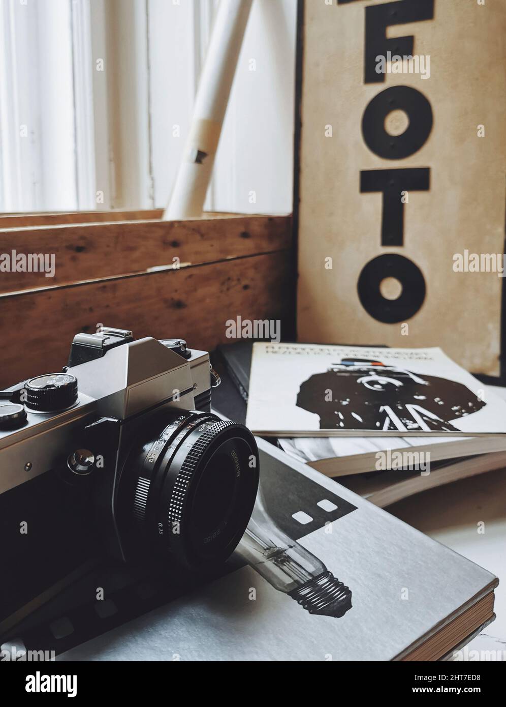 Silver and black vintage camera on books and magazines on a window sill ...