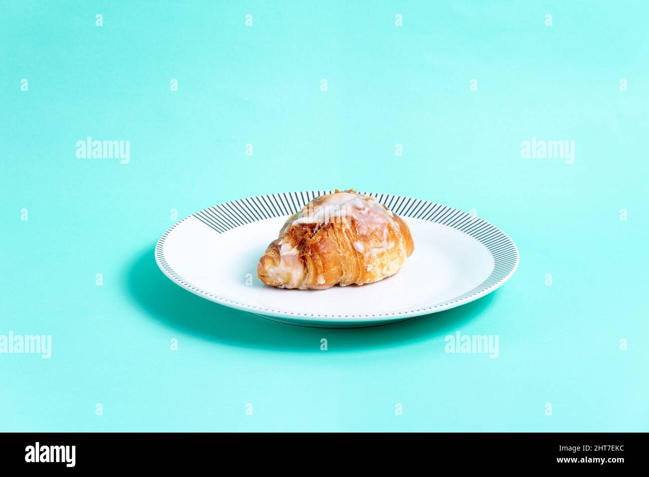 Closeup of a croissant on a white plate isolated on a green background ...