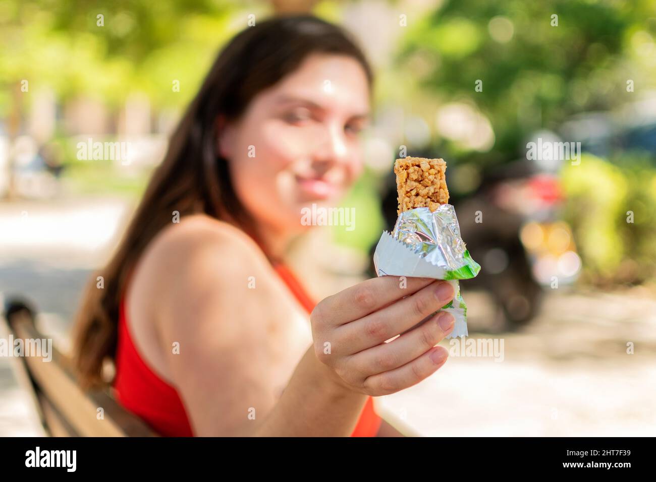 Closeup of a woman sitting on a bench and holding a snack bar at public ...