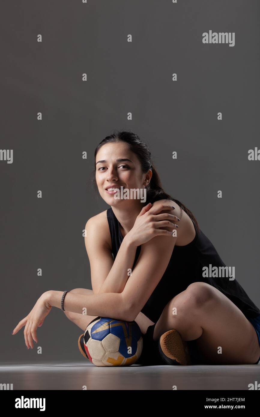 Handball player sitting on the ground. Girl posing with ball and making ...