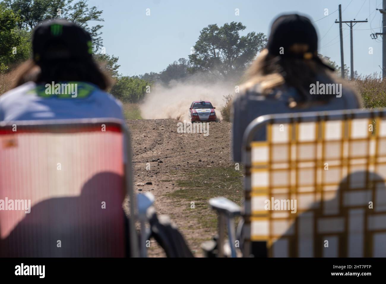 Closeup of a group of spectators watching a car race through a dirt ...