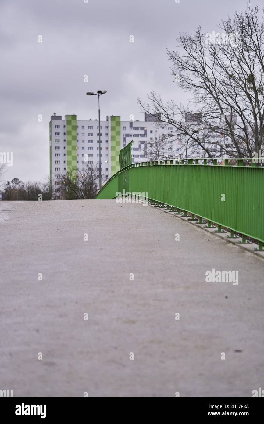 Green metal barrier on a bridge leading to a high apartment building in ...