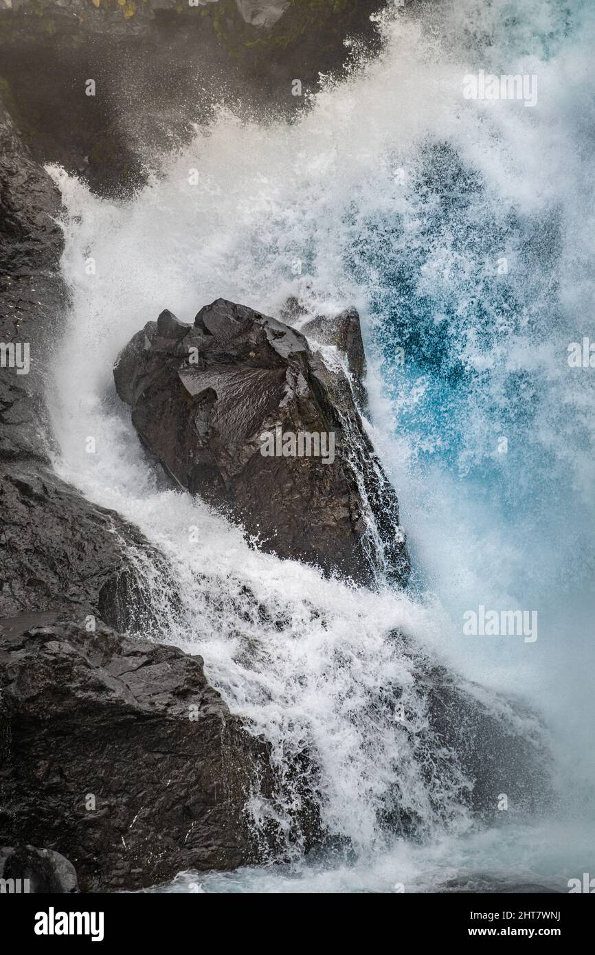 Vertical shot of a foamy waterfall splashing against black rocks ...