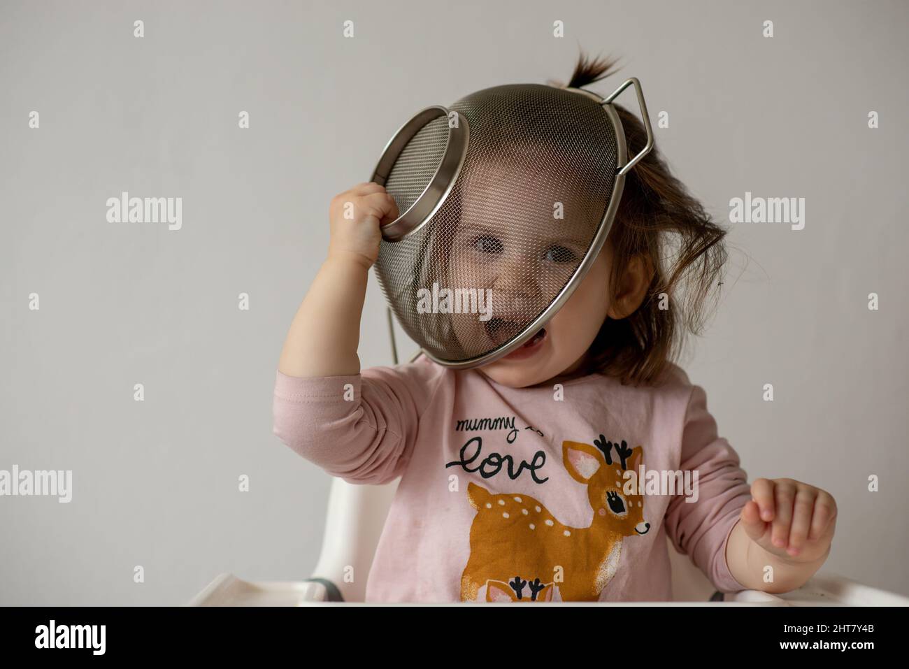 Funny baby girl covering head and face by colander, showing tongue ...