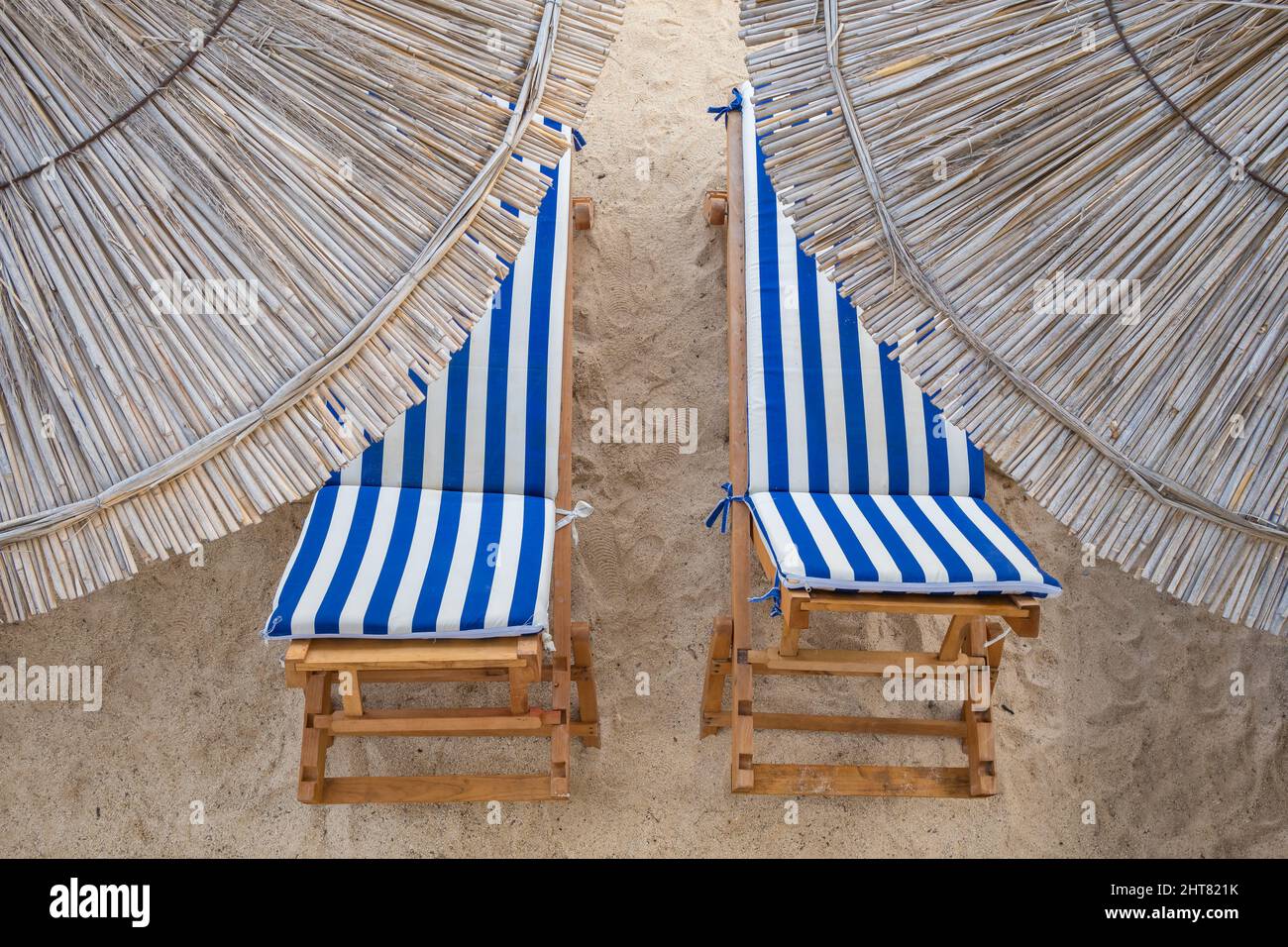 Straw beach umbrellas and two sun beds at the empty beach close-up ...