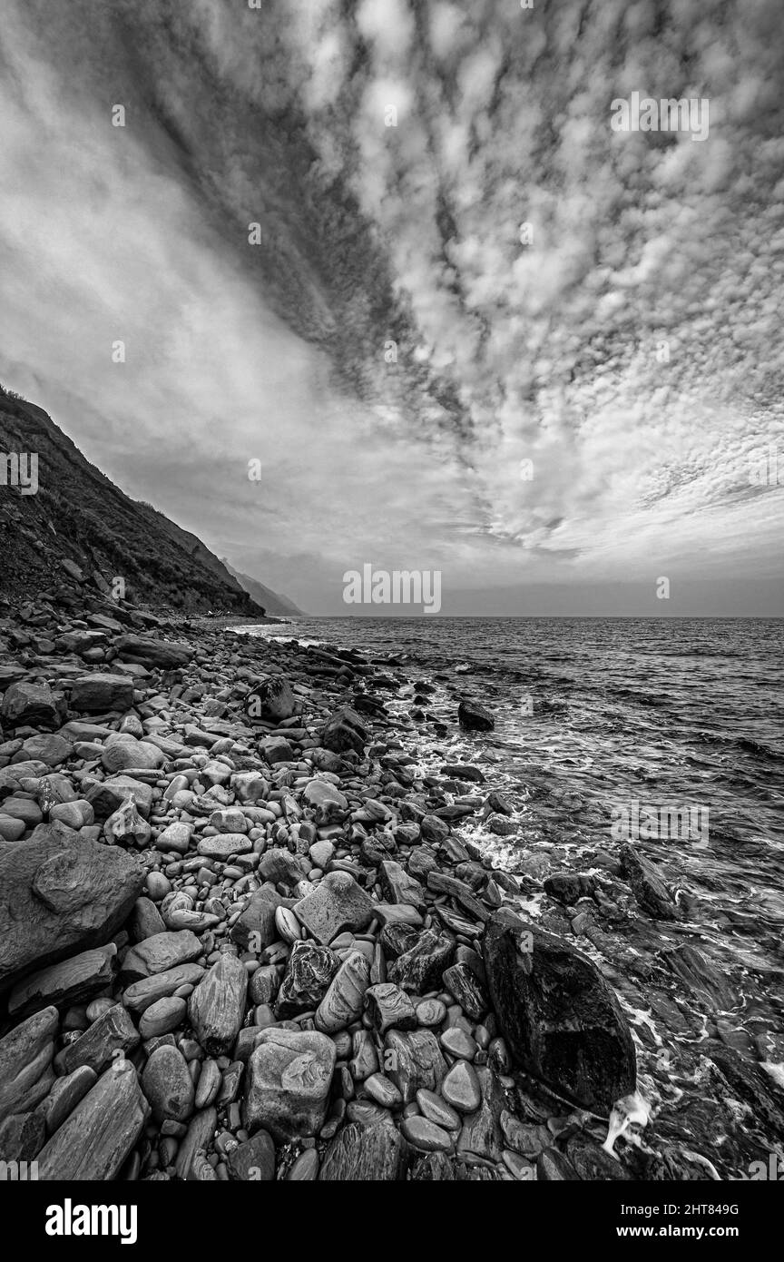 Beautiful greyscale photo of beach with pebbles, cliff, sea and cloudy ...