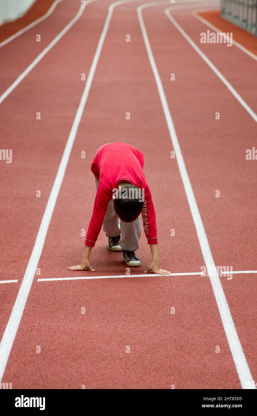 Vertical shot of a teenage guy ready to start running on a running way ...