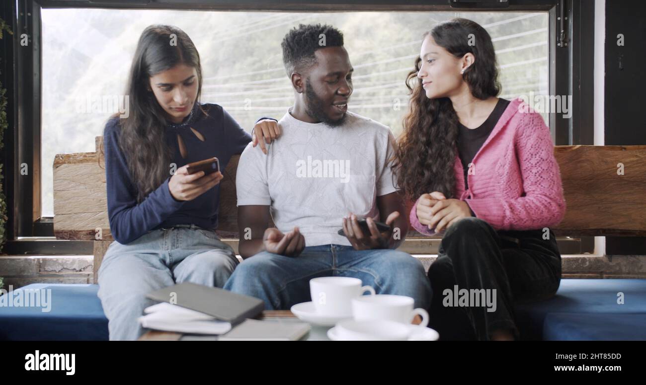 Group of Indian young people sitting on a wooden bench inside a cafe ...