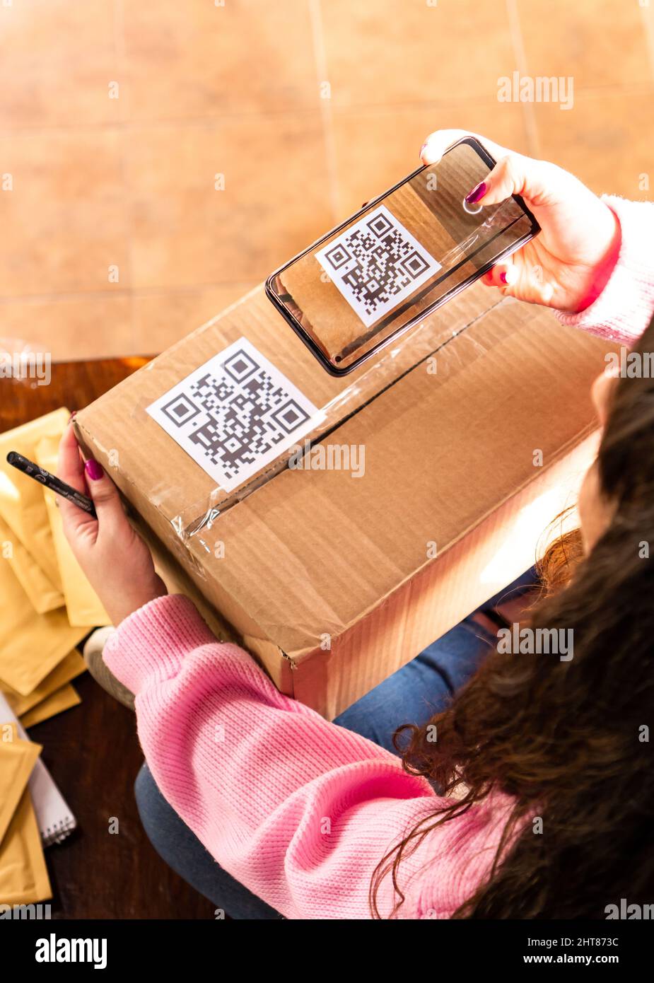 From above of crop anonymous female scanning QR code on carton box with ...