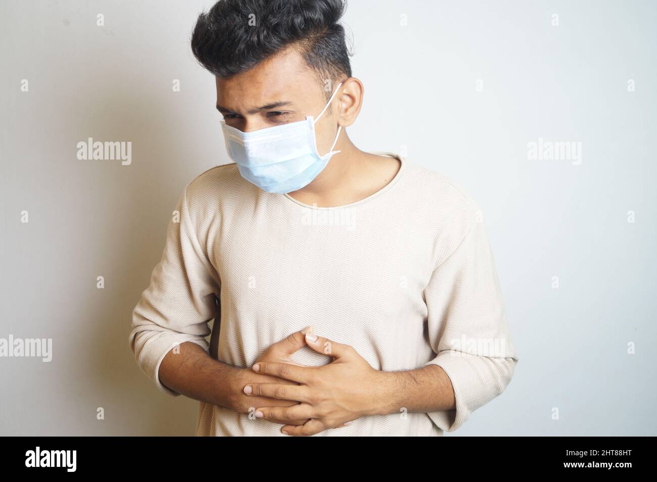 A young man holding his stomach wearing a surgical mask Stock Photo - Alamy