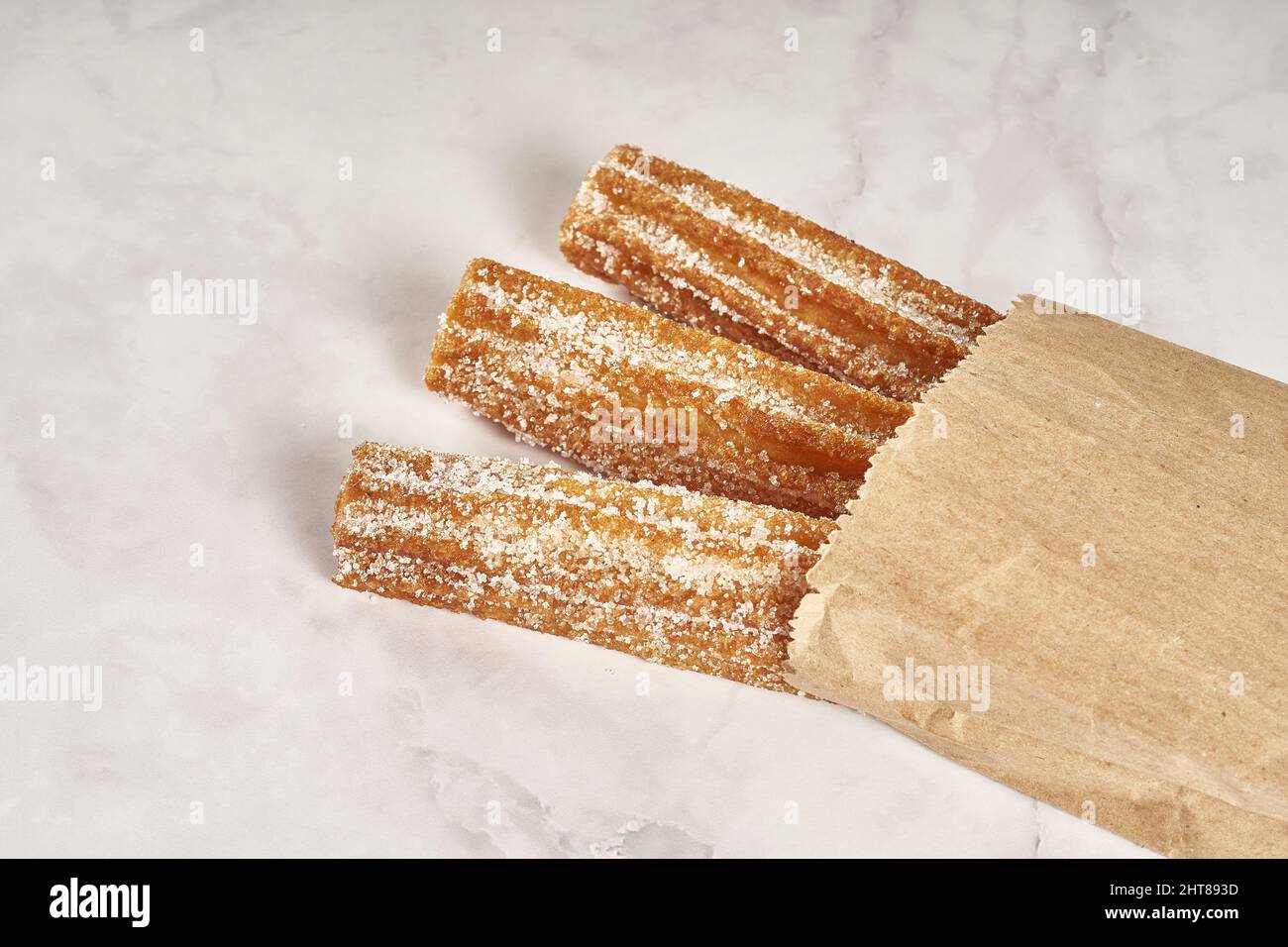 Close up shot of churros coming out of paper bag on white marble Stock ...