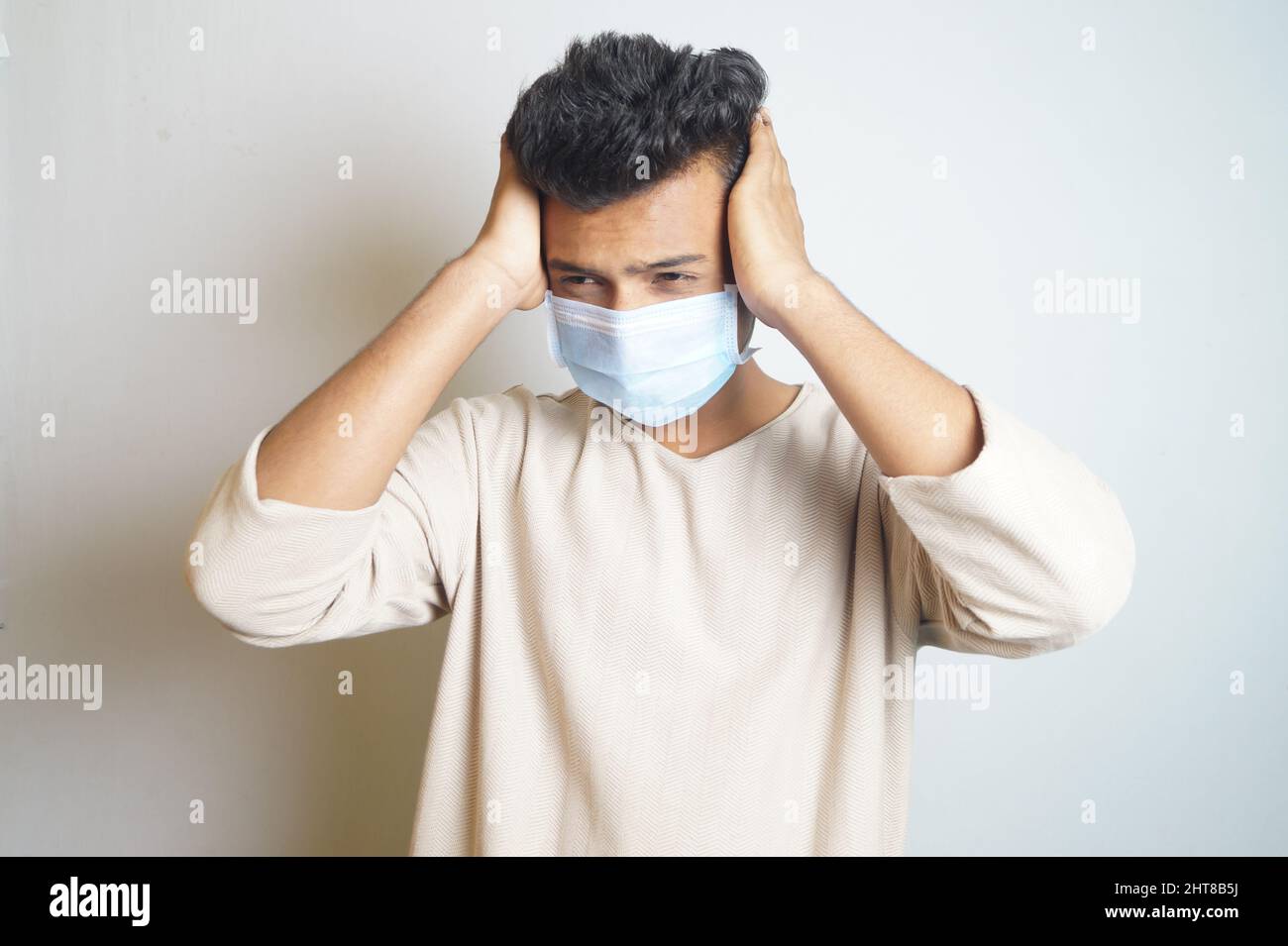 Young man holding his head and wearing a surgical mask Stock Photo - Alamy