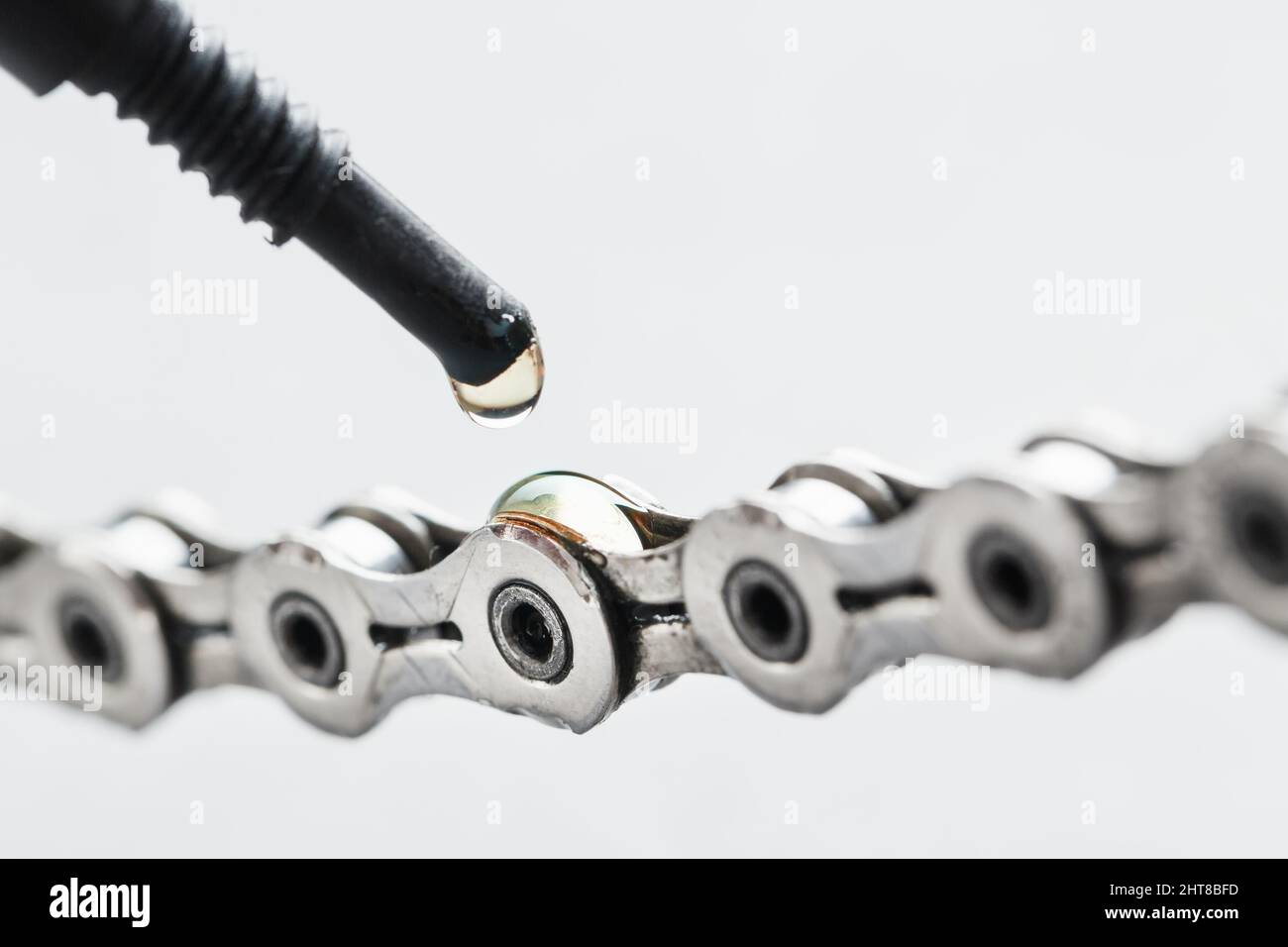 Greasing a bicycle chain with a drop of golden oil close-up on a gray ...