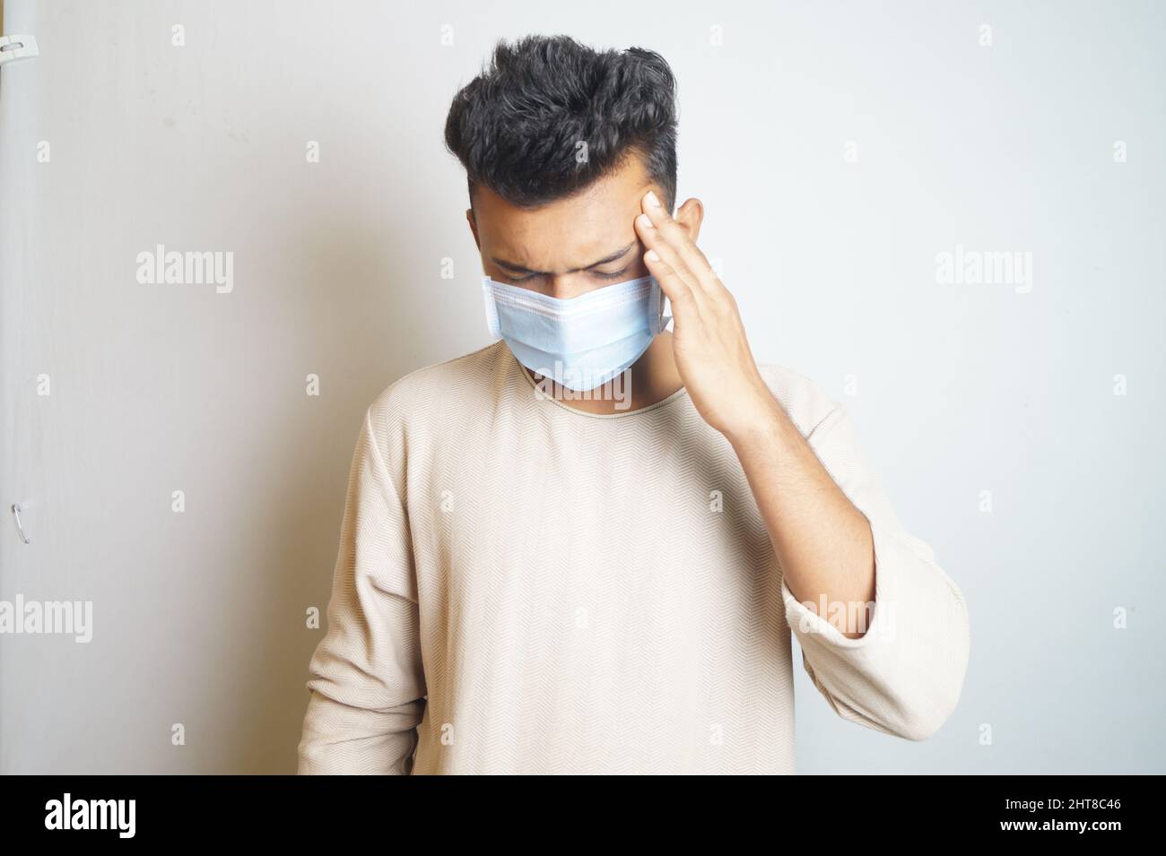 Young man wearing a surgical mask holding his head Stock Photo - Alamy