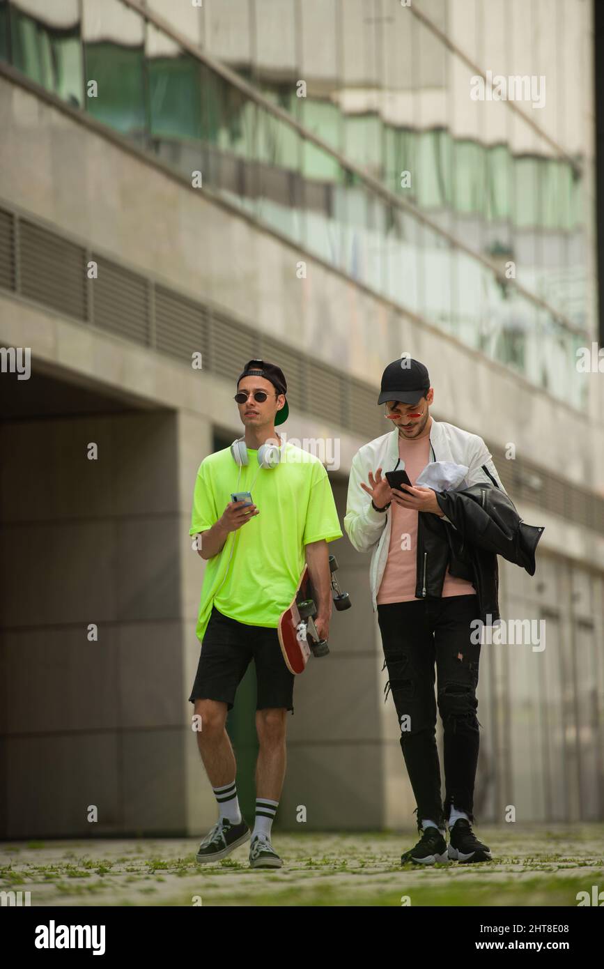 Two guy friends are walking and talking together while checking theie ...