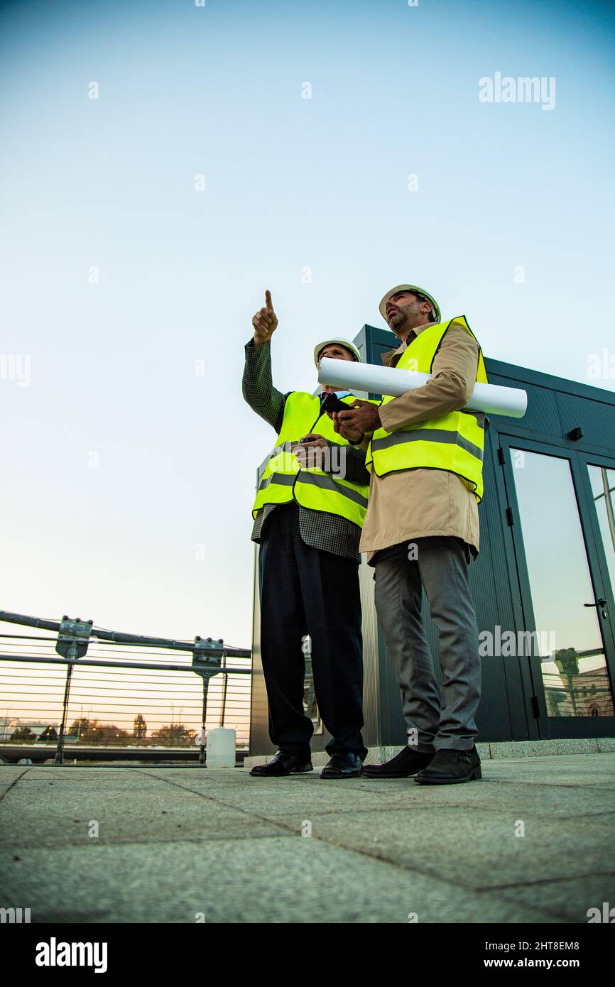Two senior construction managers are standing while talking about the ...