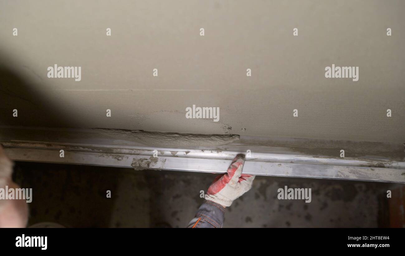 The worker levels the wall with wire. The builder is rubbing the wet ...