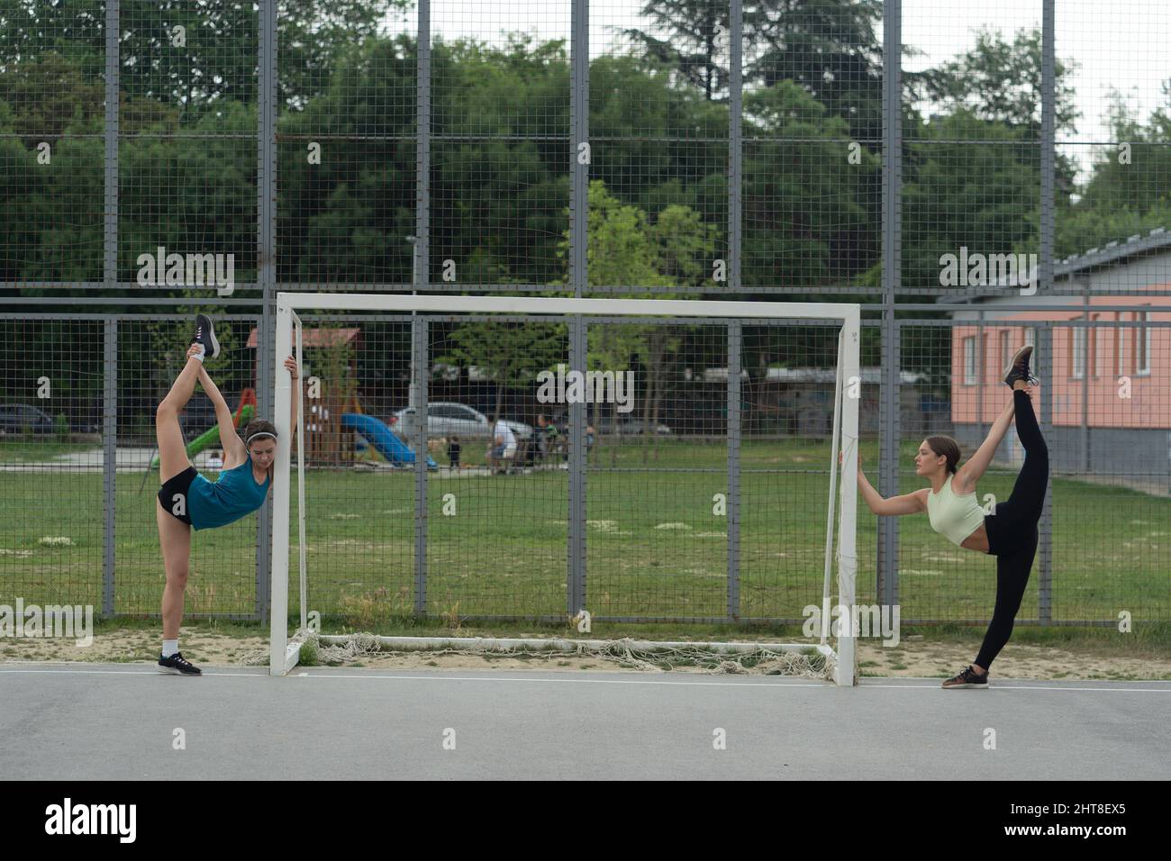 Two girls are stretching their leg up together while holding on the ...