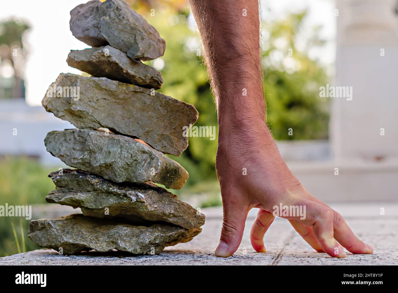 Closeup of the hand of a man with a column of six granite stones placed ...