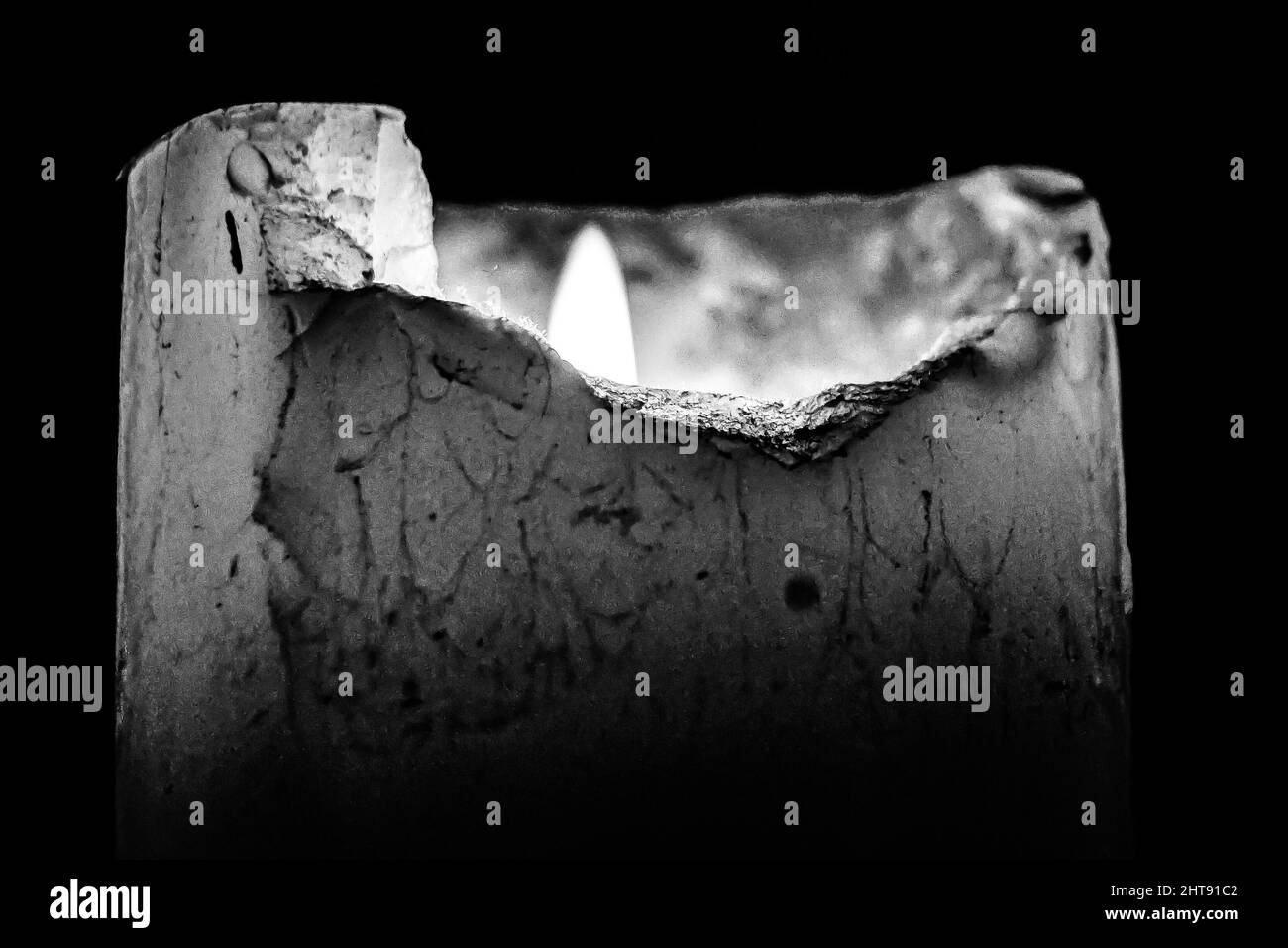Grayscale shot of an old burning candle isolated on a dark black ...