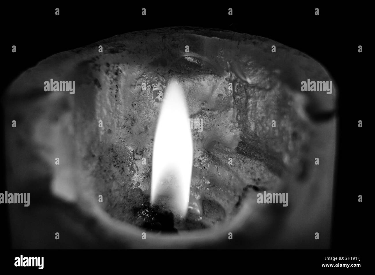 Grayscale shot of an old burning candle isolated on a dark black ...