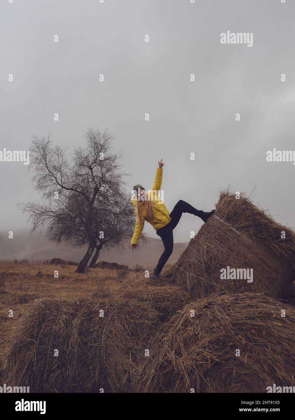 A woman poses with her leg on a haystack and her fingers pointing in ...