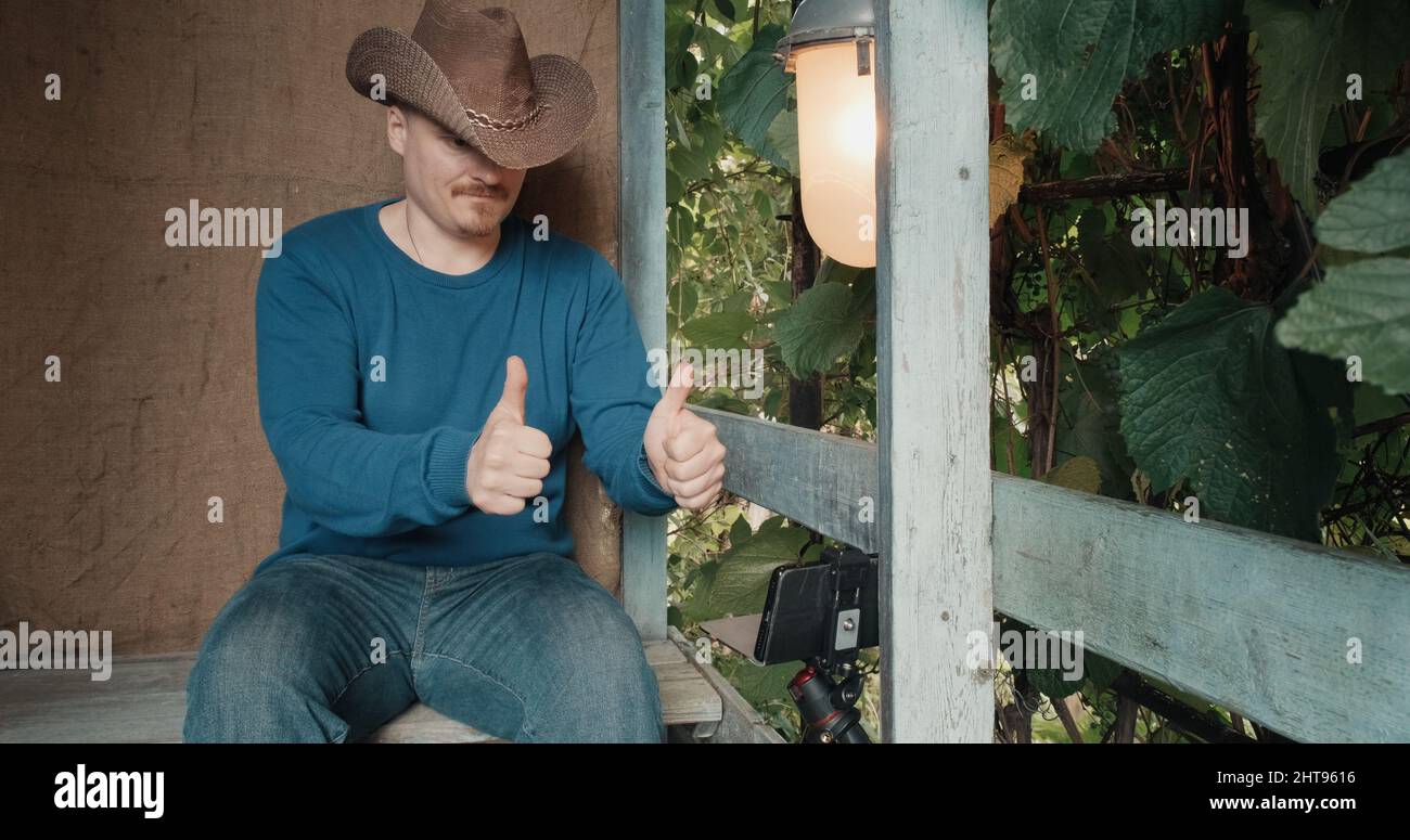Cowboy man communicates online using his phone while sitting on porch ...